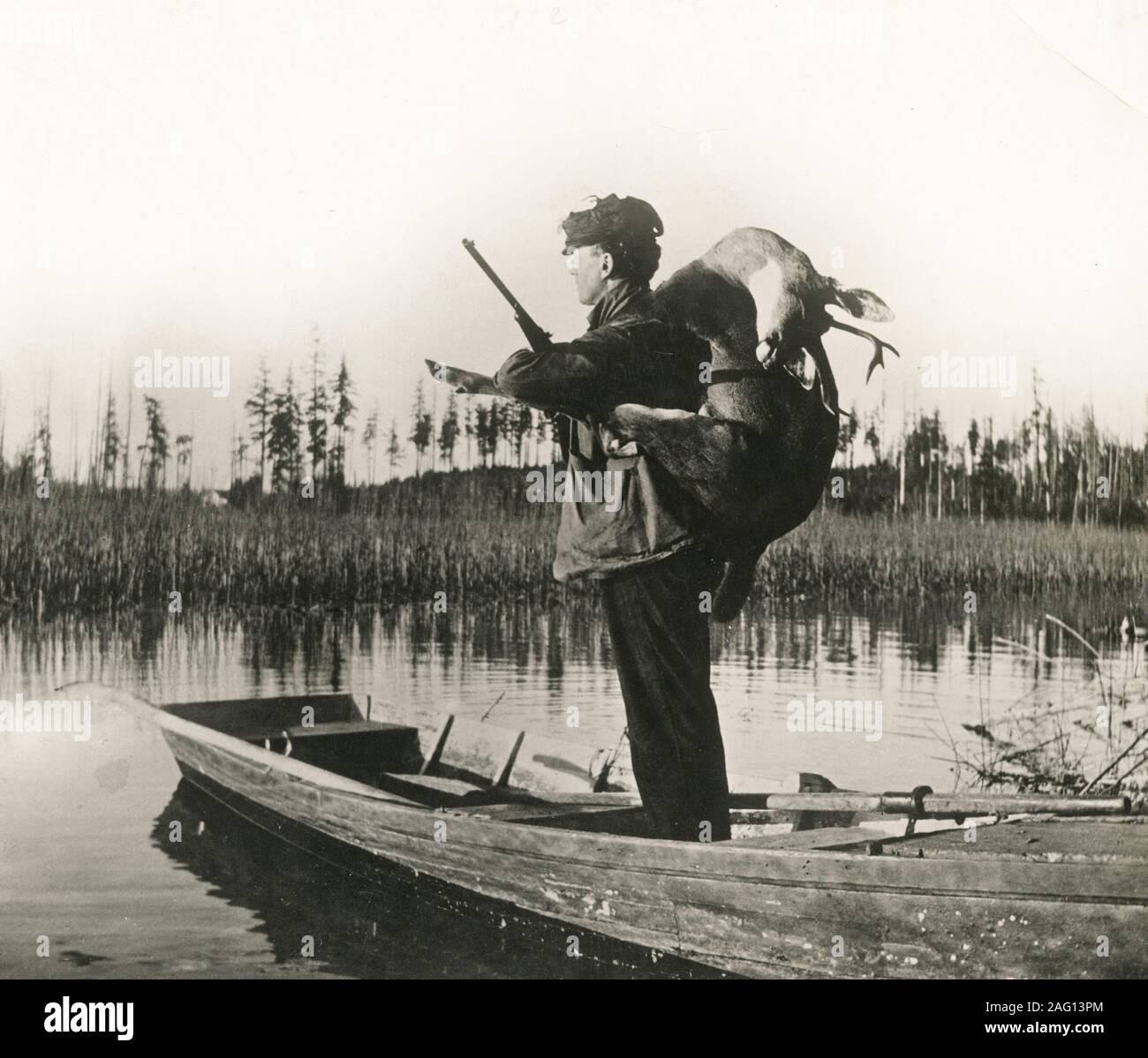 Canadian hunter on a punt with his gun and a dead deer - c.1920 Stock ...