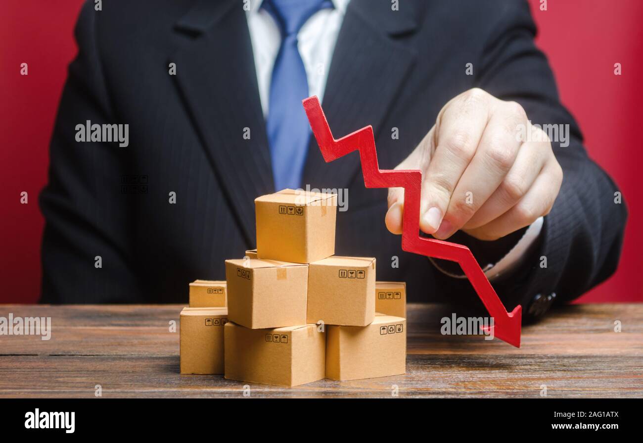 Businessman is holding a red arrow down above boxes stack pile ...