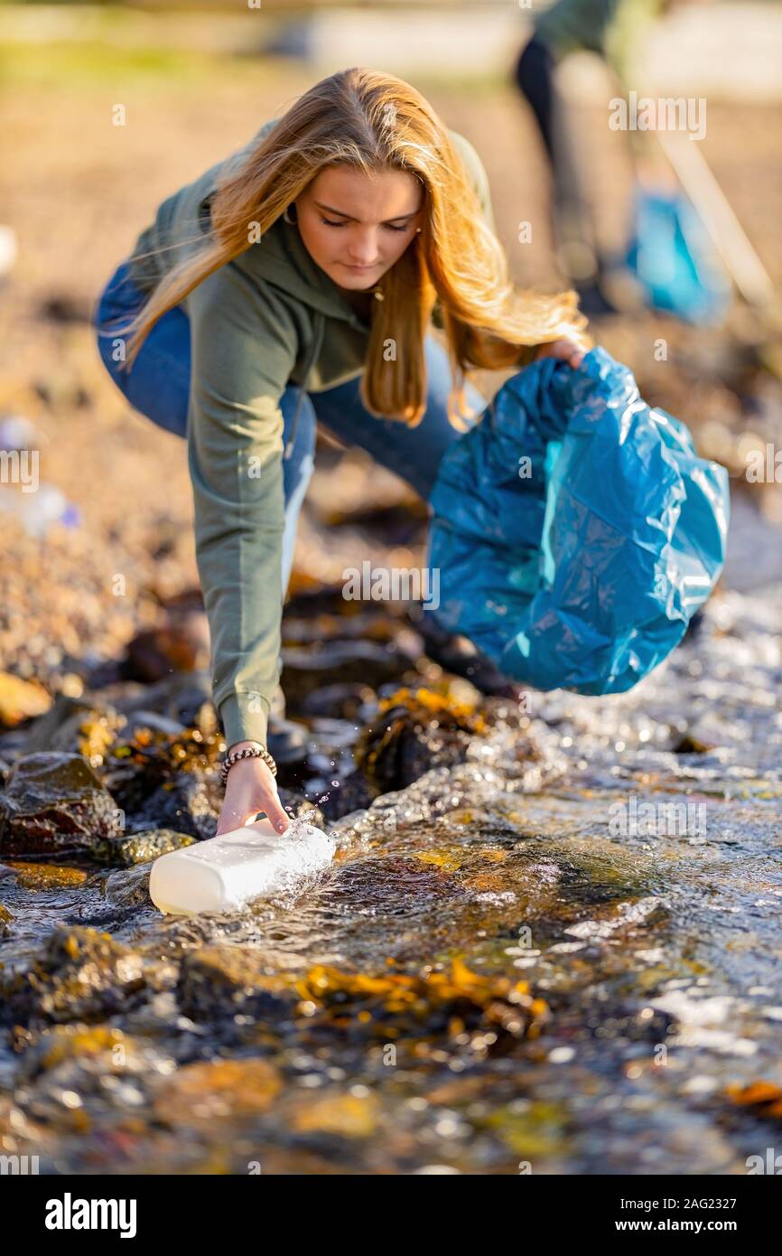 Young woman picking up garbage from rocky shore Stock Photo - Alamy