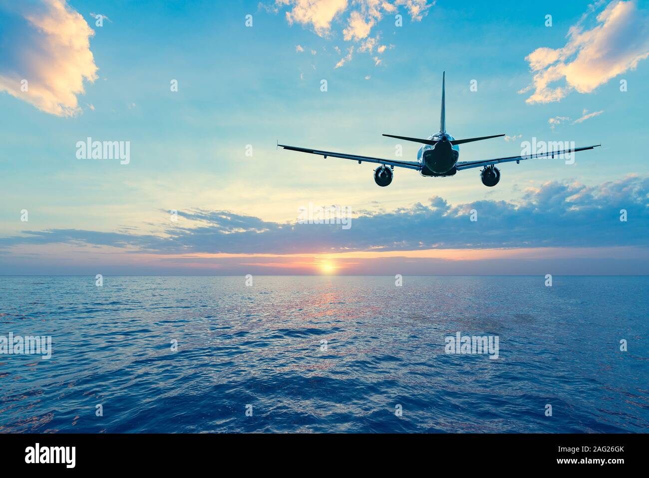 Flying of the passenger plane above the sea surface at sunset time ...