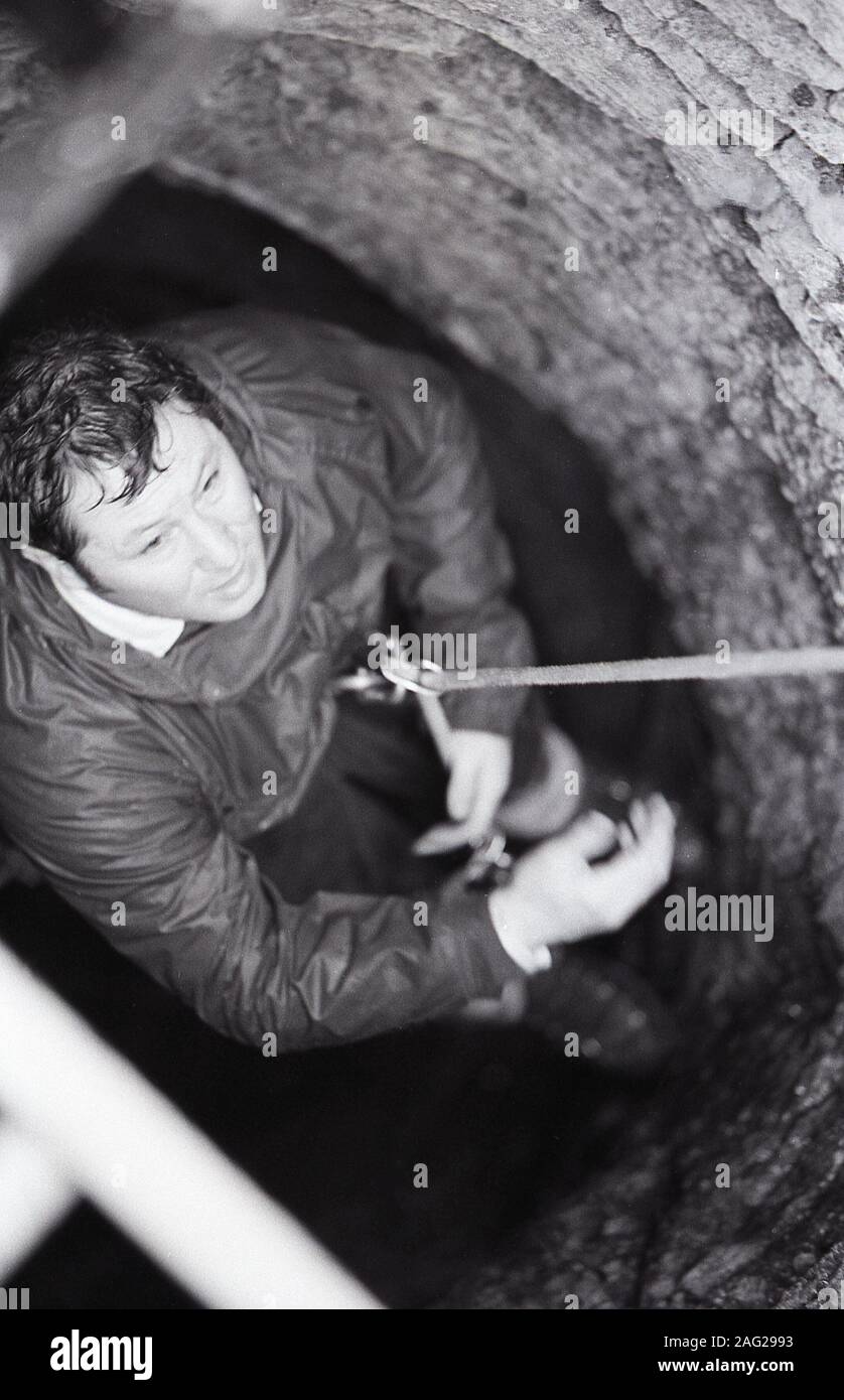1980s, historical, a man in an old water well, with a rope around him ...