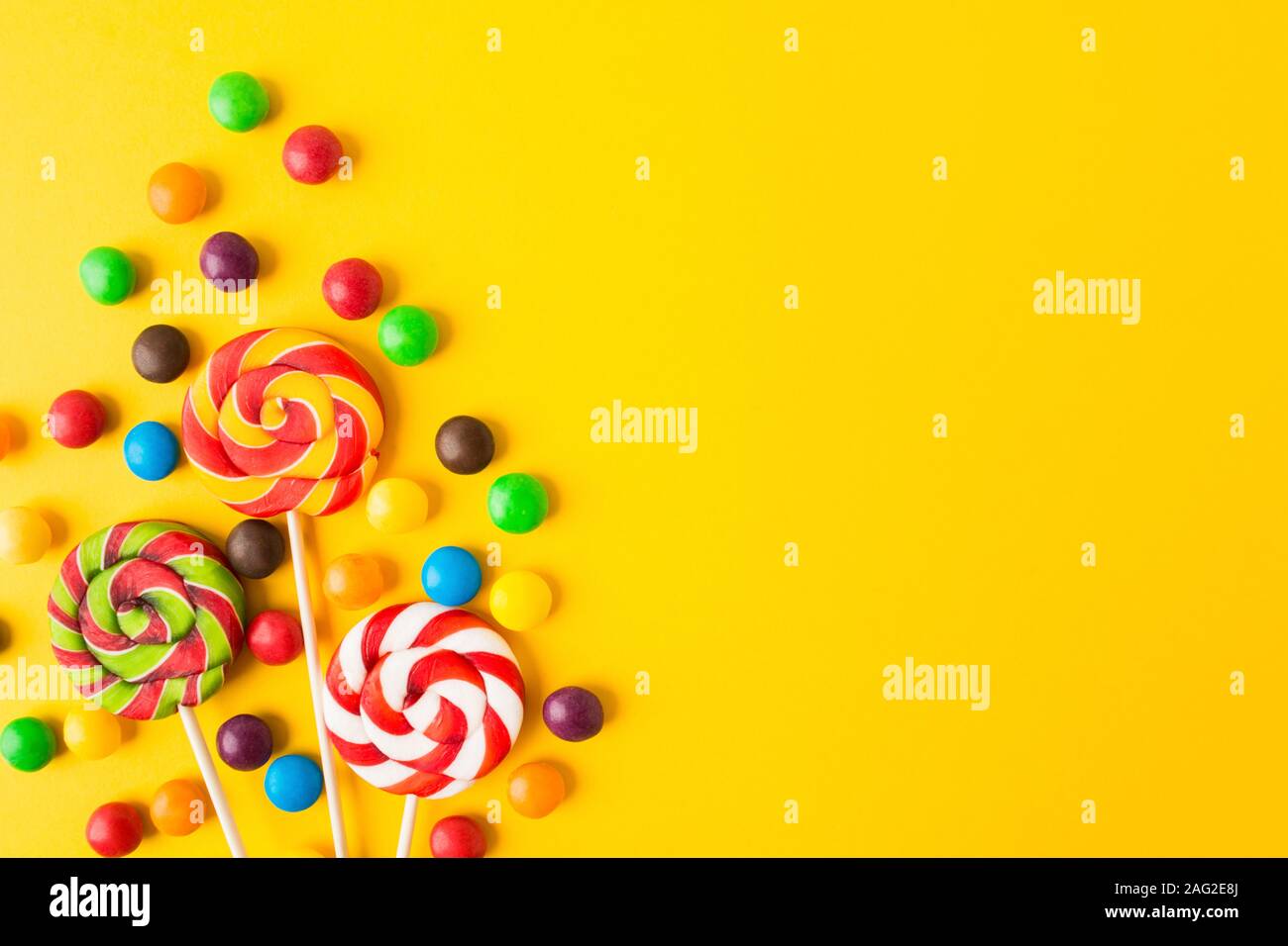 Three colorful round candies on sticks over yellow background with copy ...