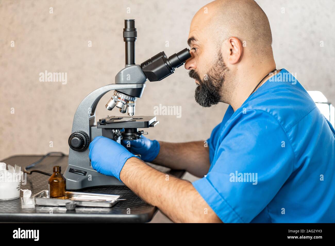 Male laboratory assistant examining biomaterial samples in a microscope ...