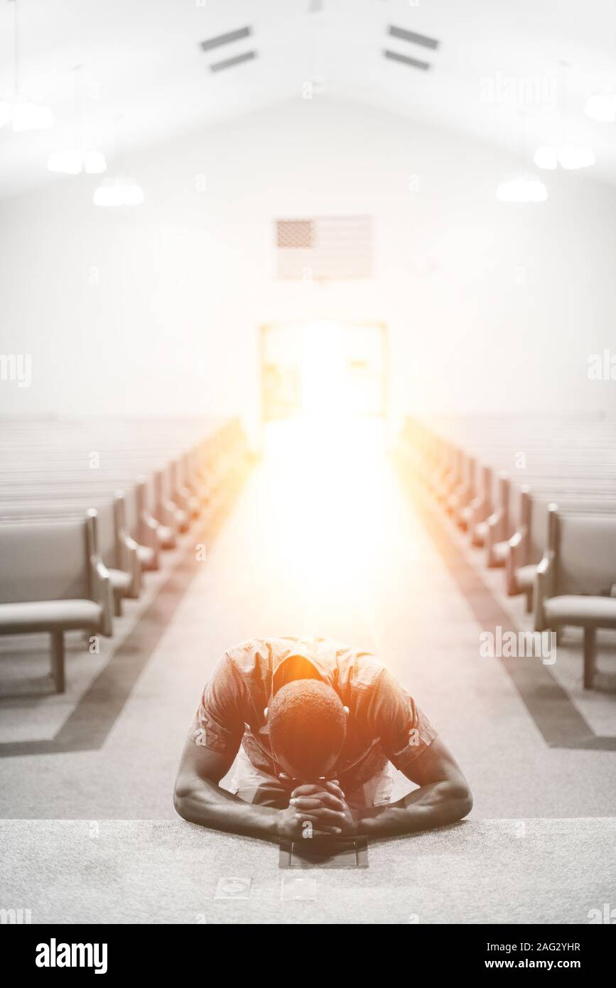 Vertical shot of a male on his knee and praying in the church in black ...
