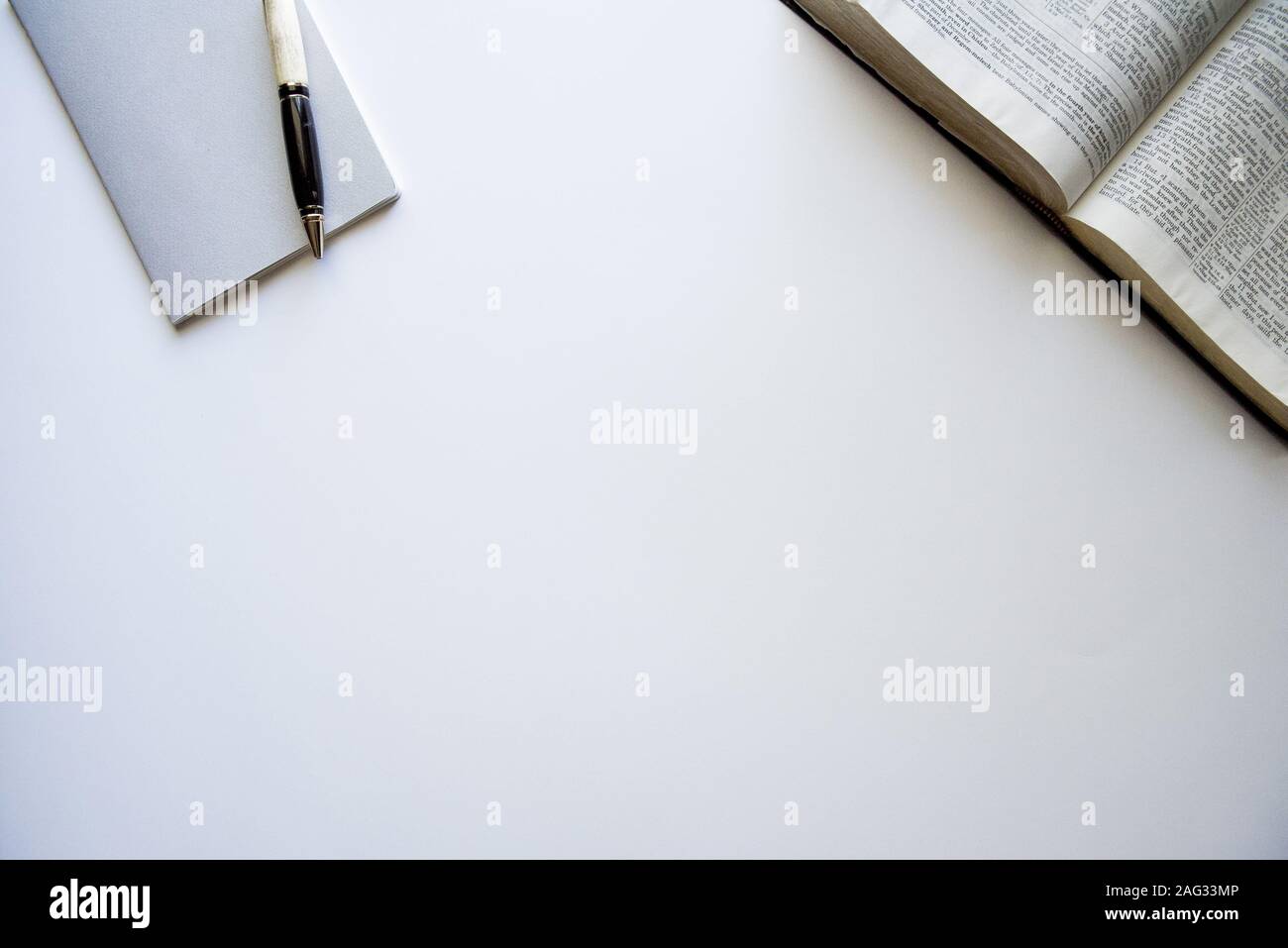 Overhead shot of an open bible and a notepad with a pen on a white ...