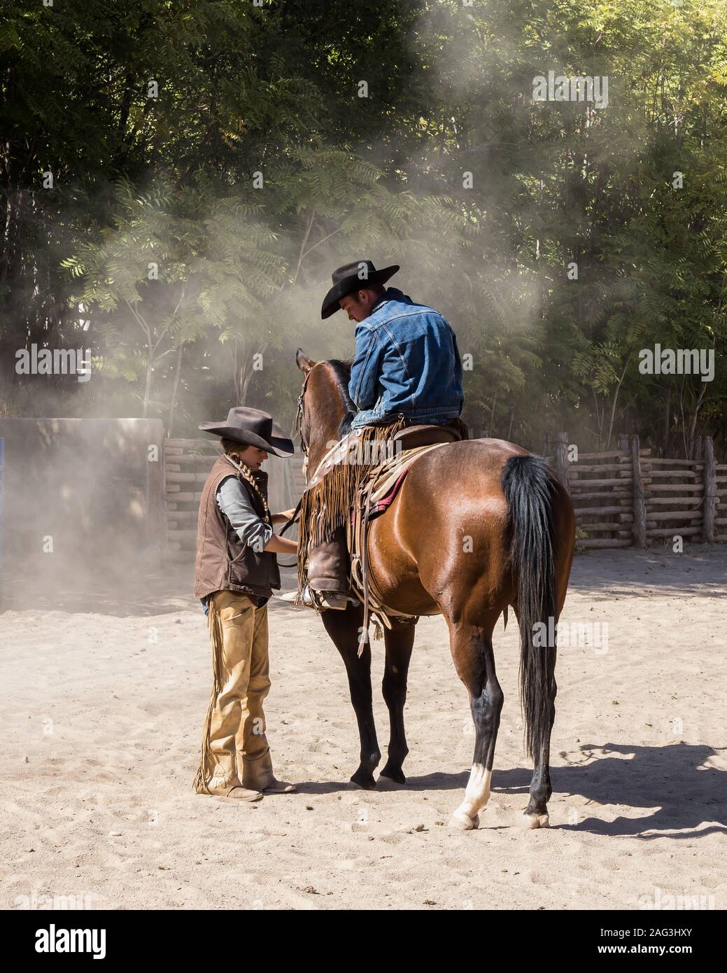 A cowgirl adjusts the saddle rigging for one of the cowboys on a ranch ...