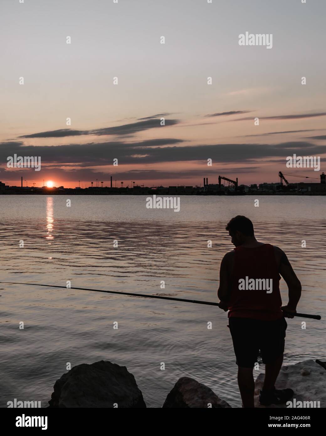 Vertical shot of a fisherman fishing by the sea with the sunset in the ...