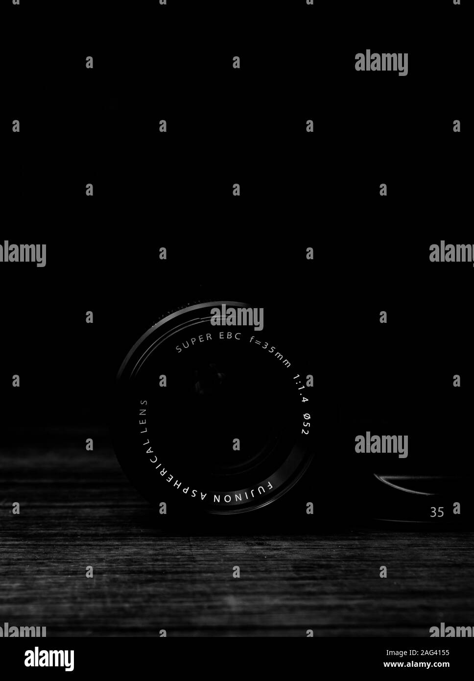 Vertical gray scale shot of a camera lens on a wooden surface Stock ...