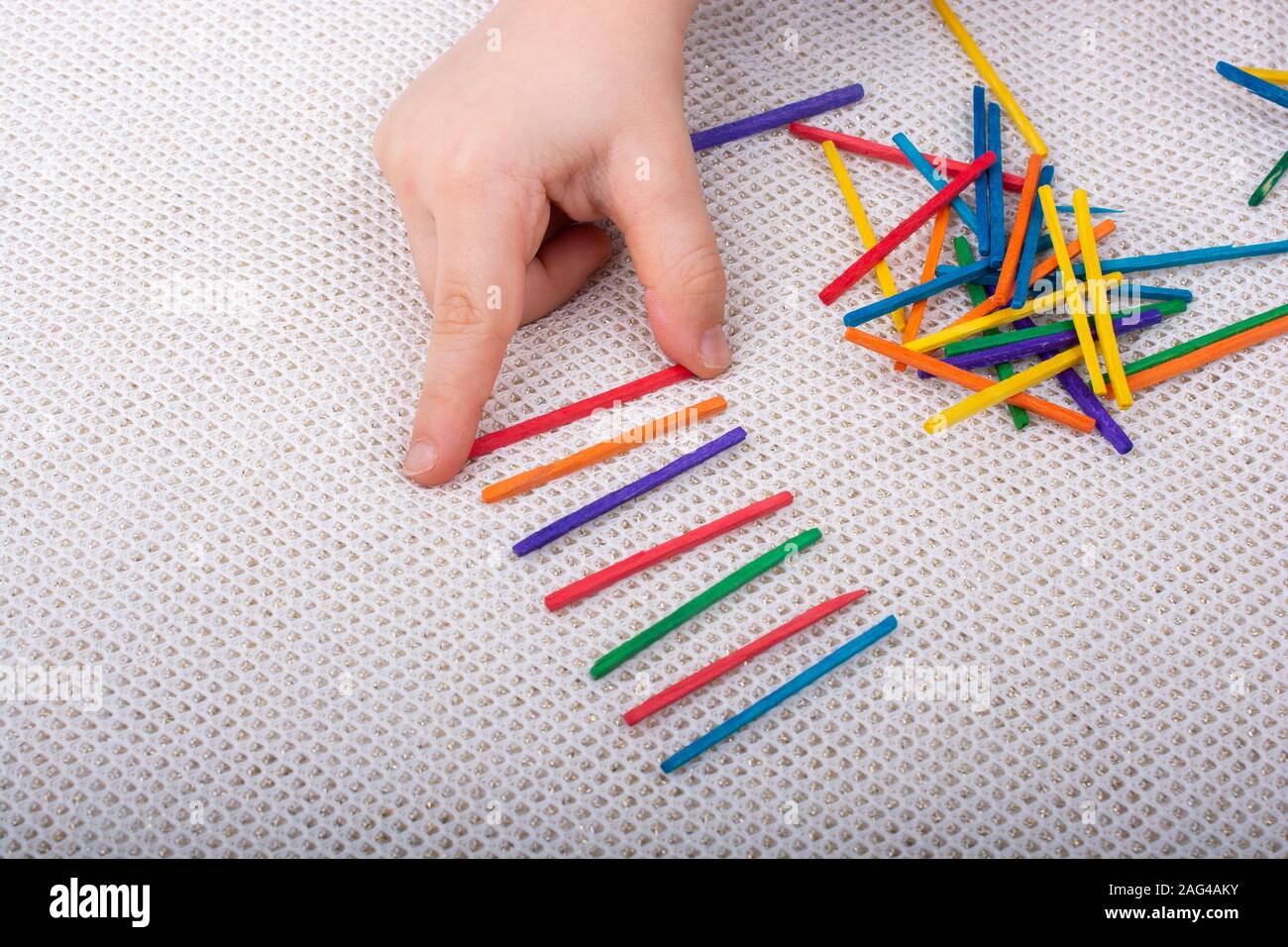 Kid playing with coloured wooden sticks for creativity on white ...