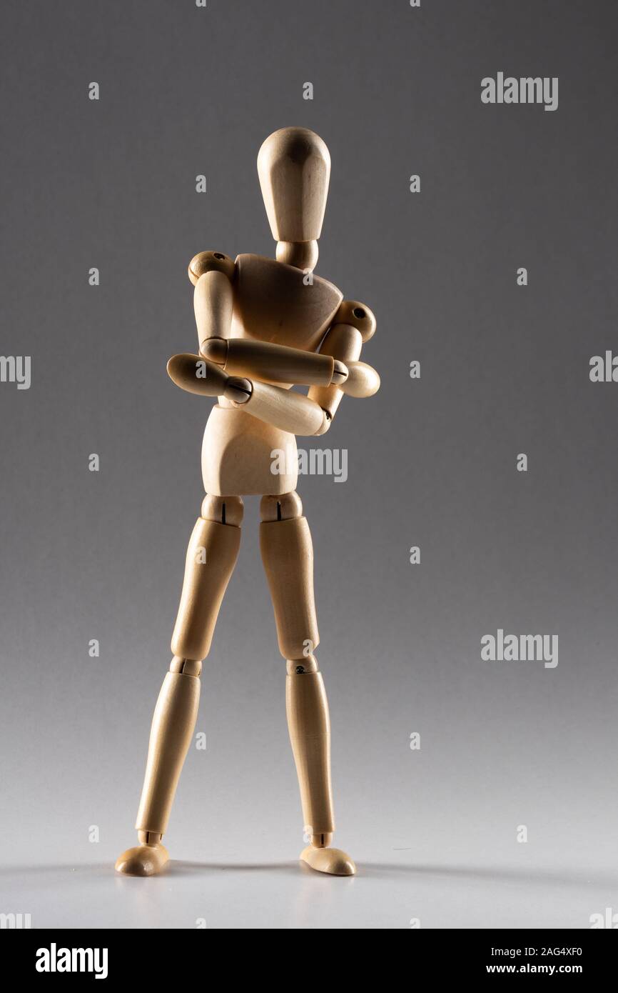 Vertical shot of a wooden pose doll with crossed arms standing in the ...