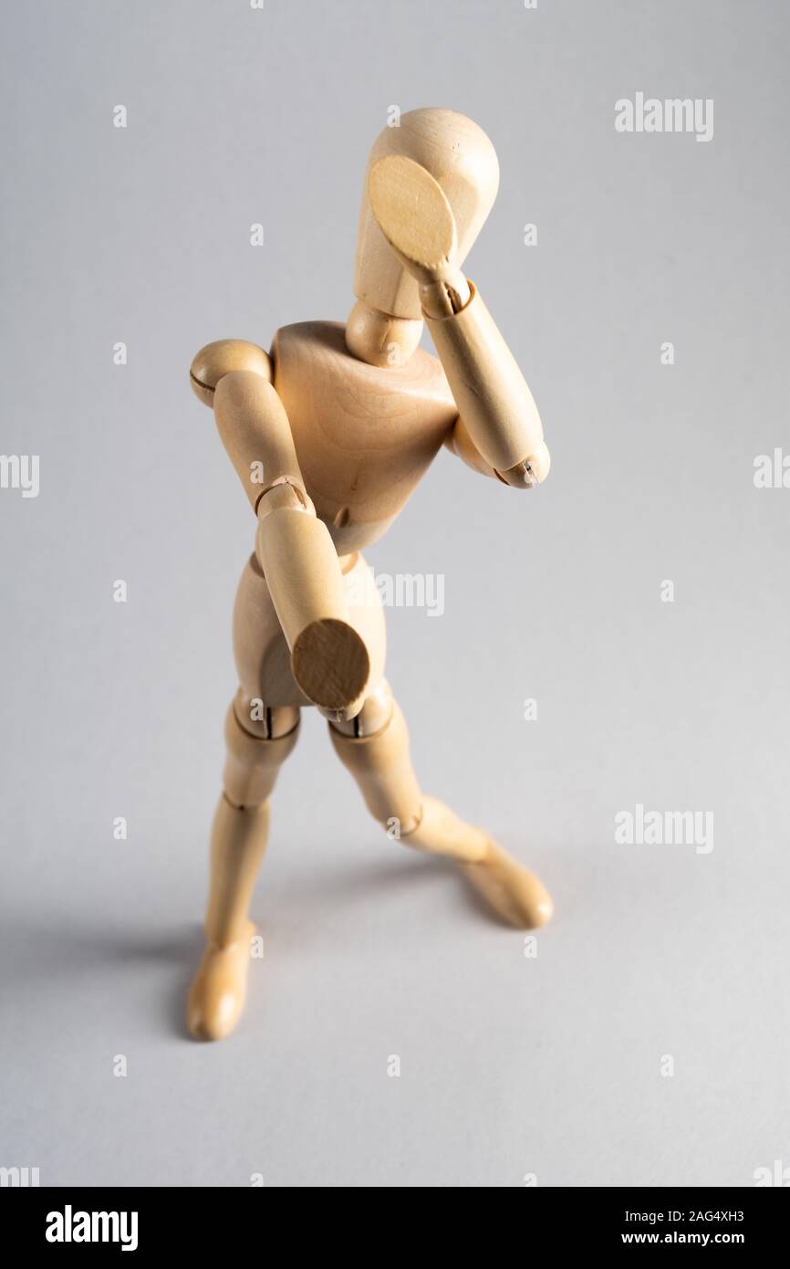 Vertical high angle shot of a wooden pose doll covering its face on a ...