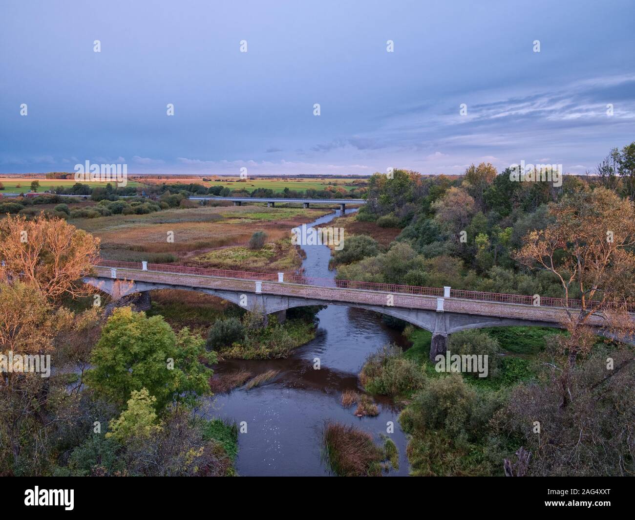 High angle shot of a long bridge over the river flowing in a field with ...