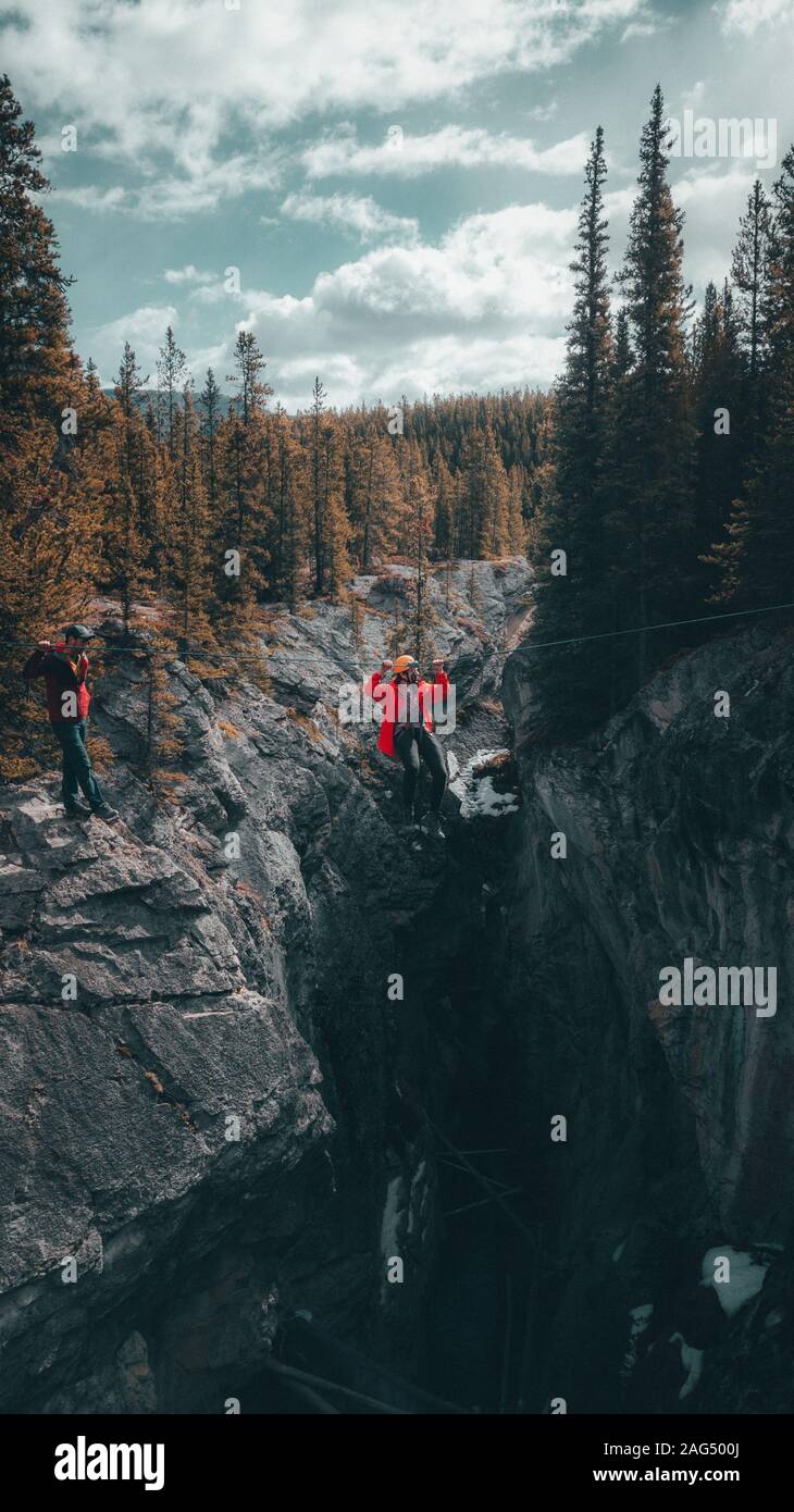 Vertical shot of two people walking on a cable between to cliffs over a ...