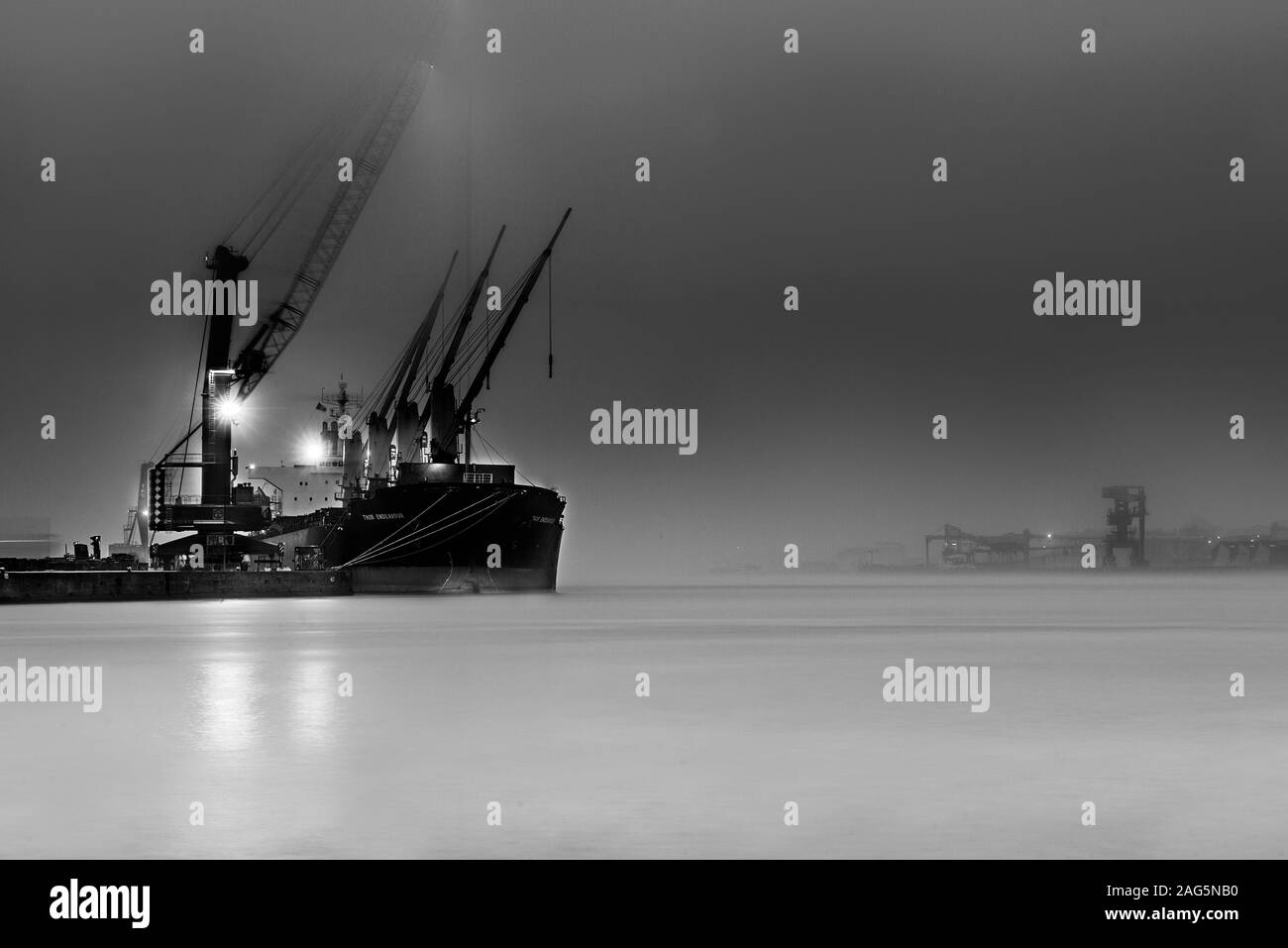 Grayscale shot of an industrial ship with lights on the sea enveloped ...