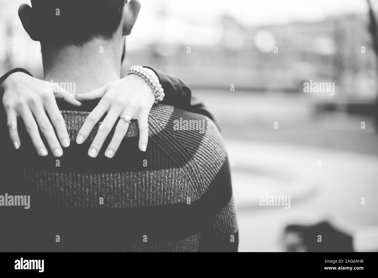 Grayscale shot from the behind of a newly engaged couple hugging with a ...