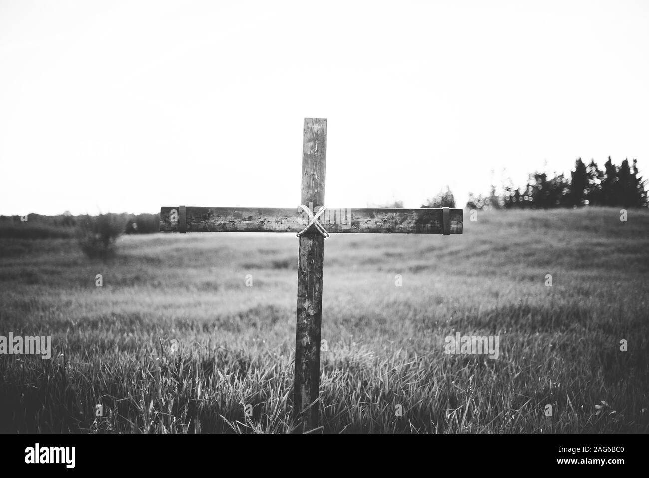 Grayscale shot of a wooden cross in a grassy field with a blurred ...