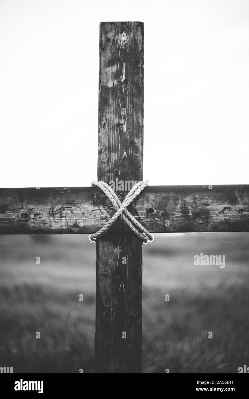 Vertical grayscale shot of a rope wrapped around a wooden cross with a ...