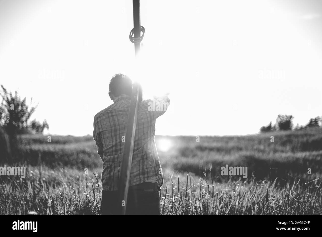 Grayscale shot from behind of a male carrying a wooden cross in a ...