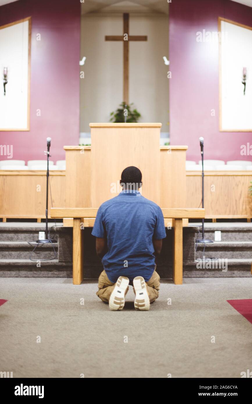 Vertical shot of a male down on his knees praying in the church ...