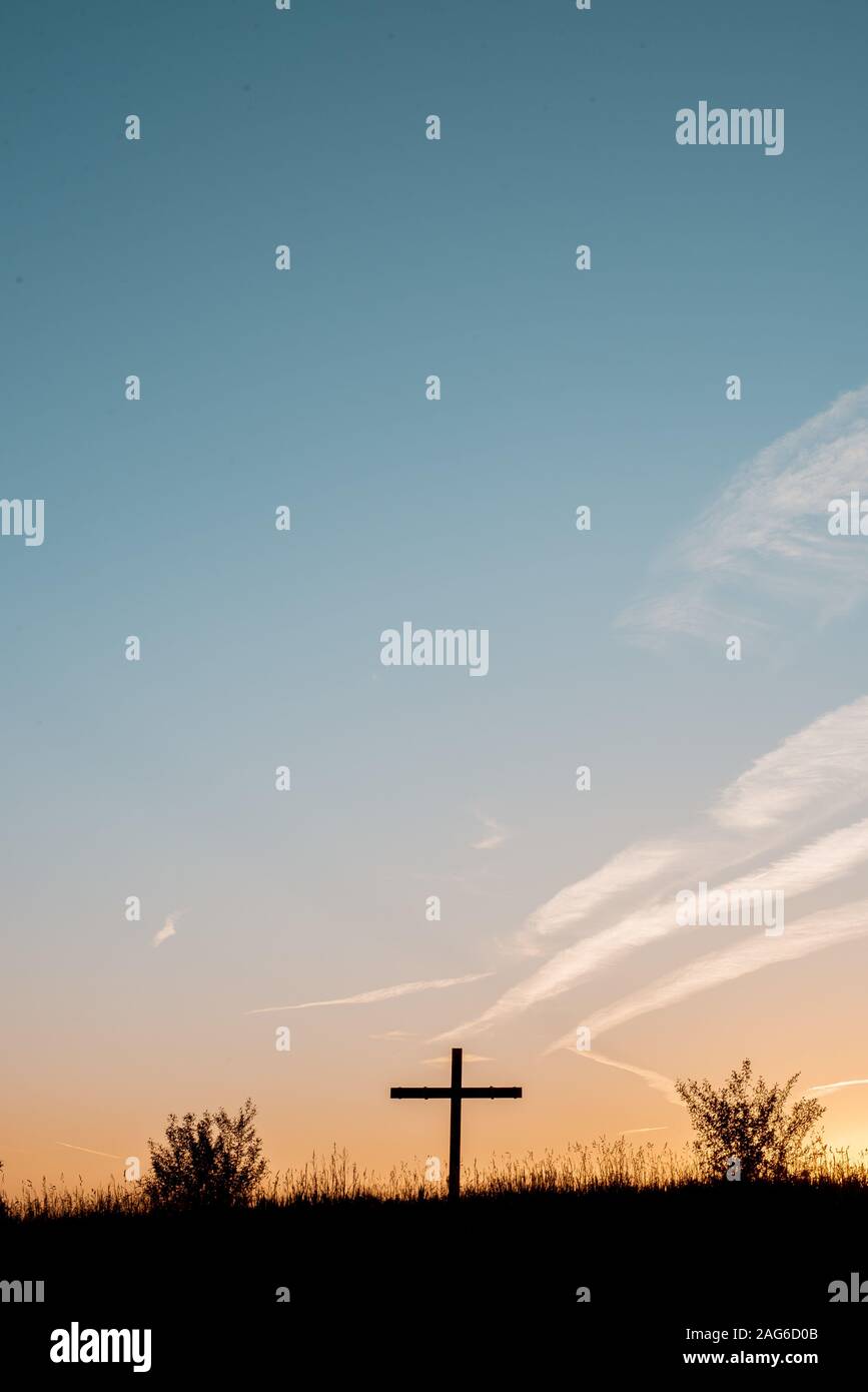 Silhouette of a wooden cross on a grassy hill with a beautiful sky in ...