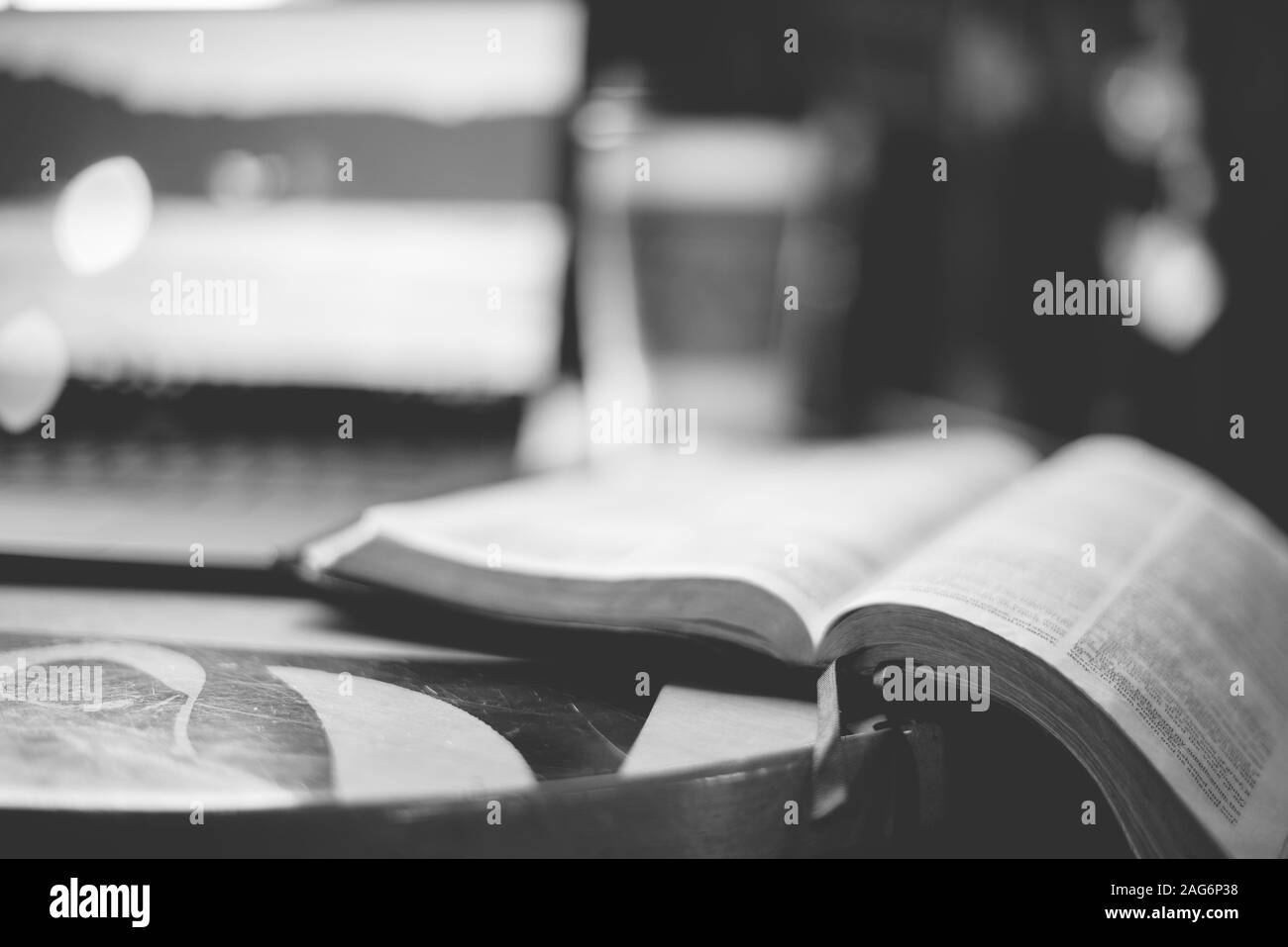 Grayscale closeup shot of an open bible on the table wit ha blurred ...