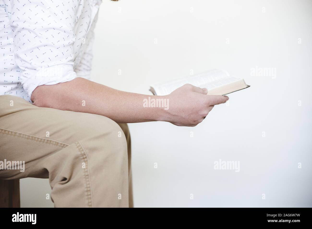 Closeup shot of a male sitting and reading the bible with a white ...
