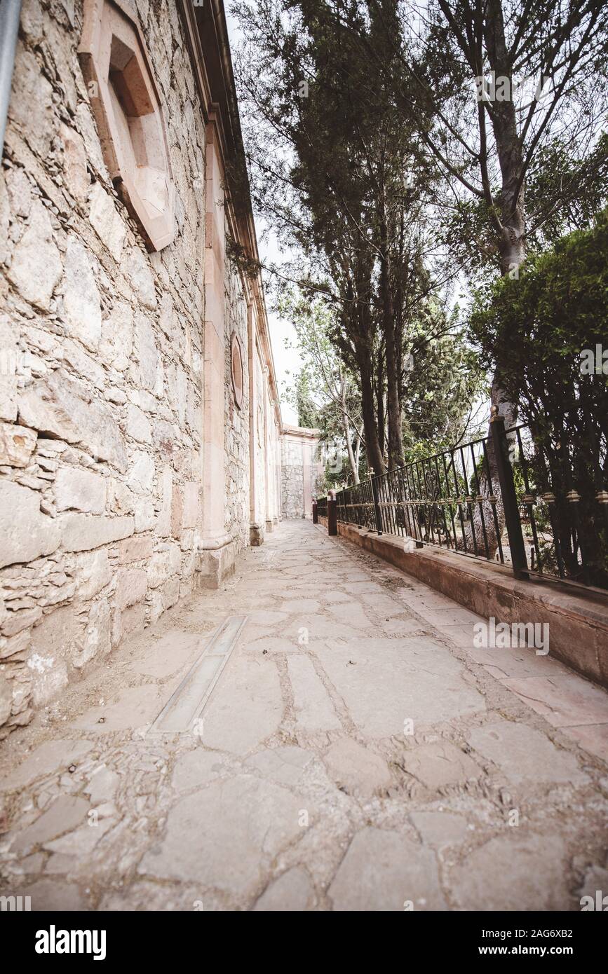 Vertical shot of an empty pathway on the side of a building near trees ...
