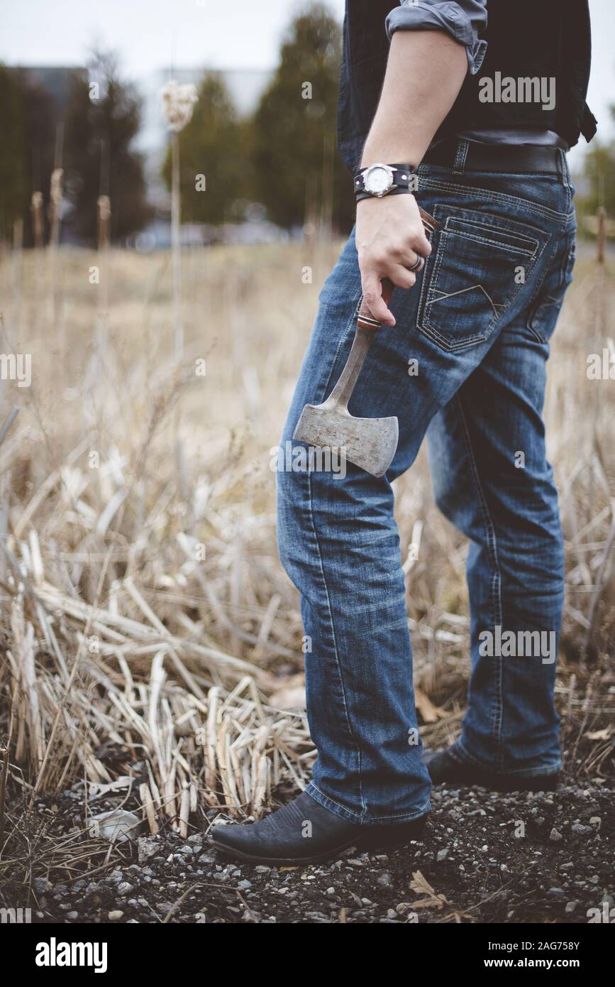 Vertical closeup shot of a male standing and holding a small ax with a ...