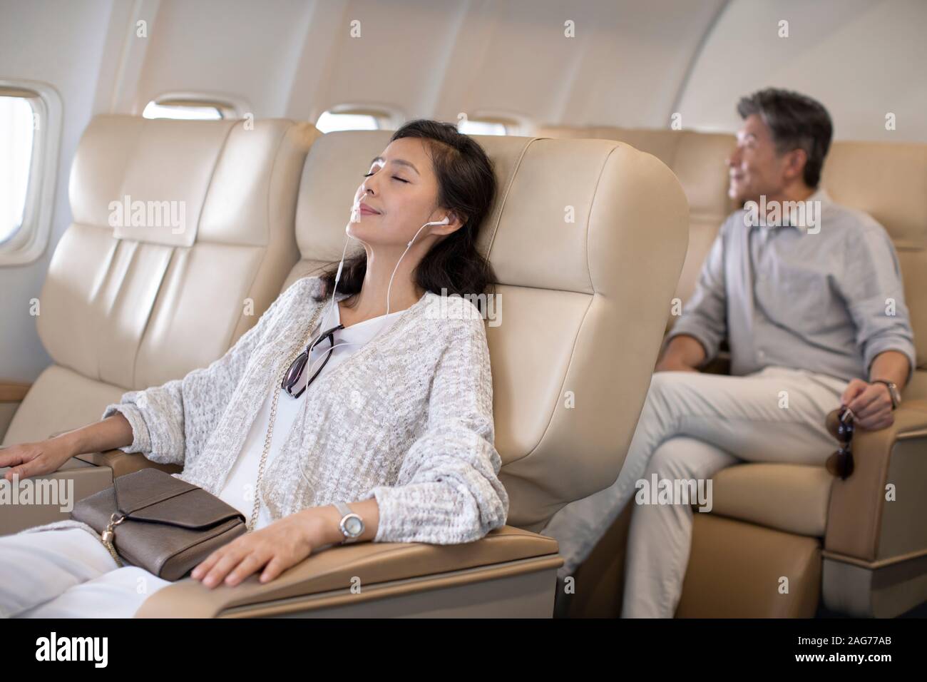Mature Chinese woman wearing earbuds during flight Stock Photo - Alamy