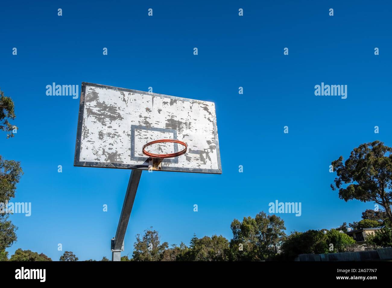 Old rusty basketball hoop above tree tops against blue sky with copy ...