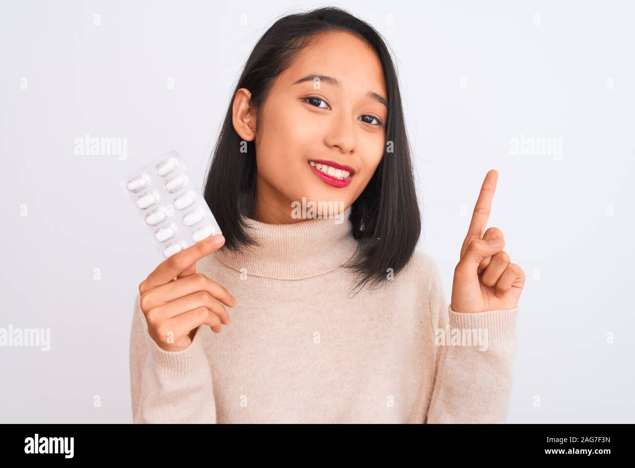 Young beautiful chinese woman holding pills standing over isolated ...