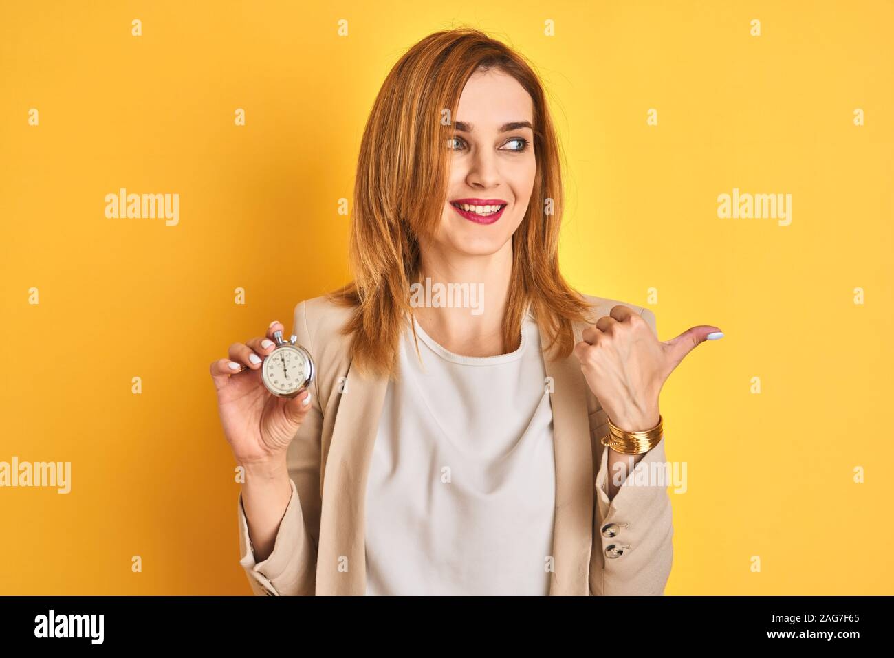 Redhead caucasian woman holding stopwatch over yellow isolated ...