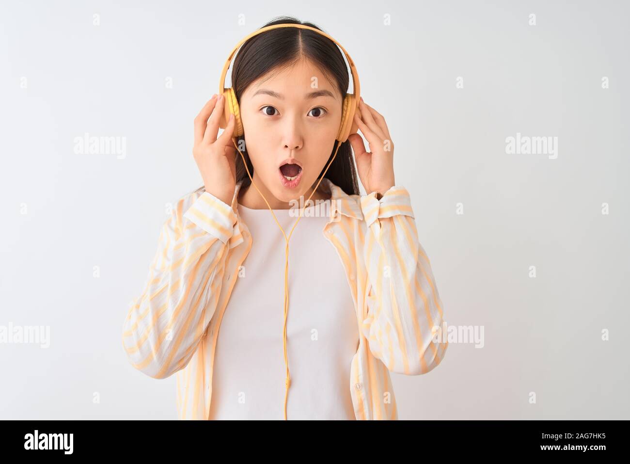 Young chinese woman listening to music using headphones over isolated ...