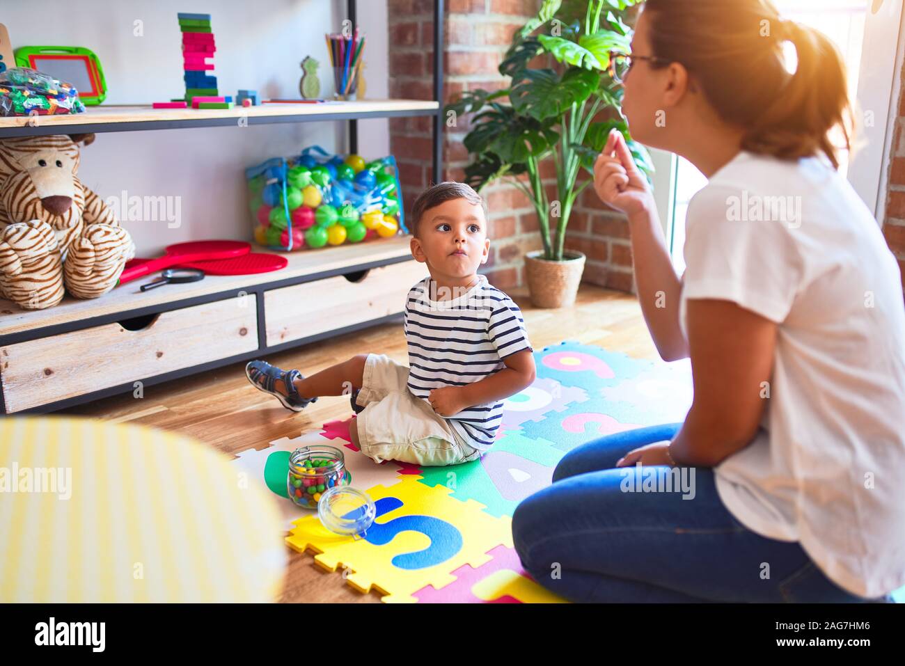Beautiful teacher and toddler boy sitting eating small chocolate balls ...