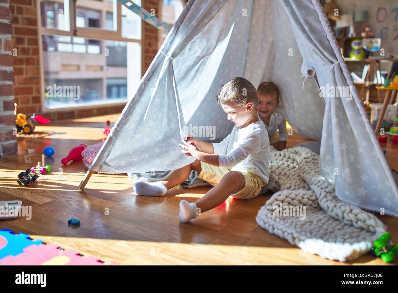 Adorable blonde twins playing inside tipi around lots of toys at ...