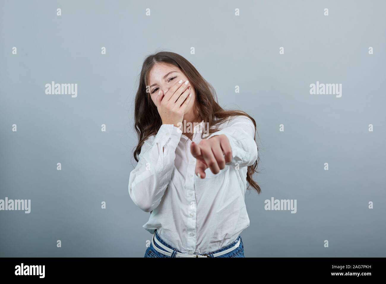 Happy young woman covering mouth with hand, pointing finger at camera ...