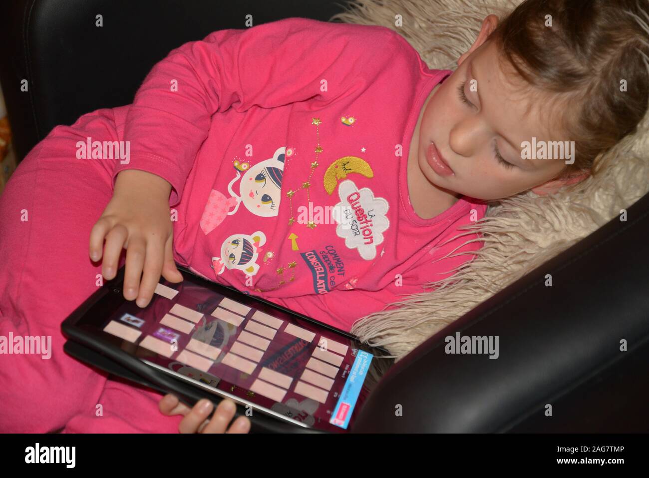 Concentred little girl in red pajamas playing with her tablet Stock ...