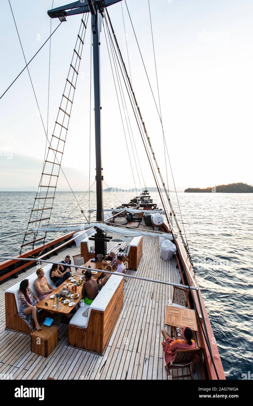Guests dining on luxury phinisi sailing cruise boat at sunset in Raja ...