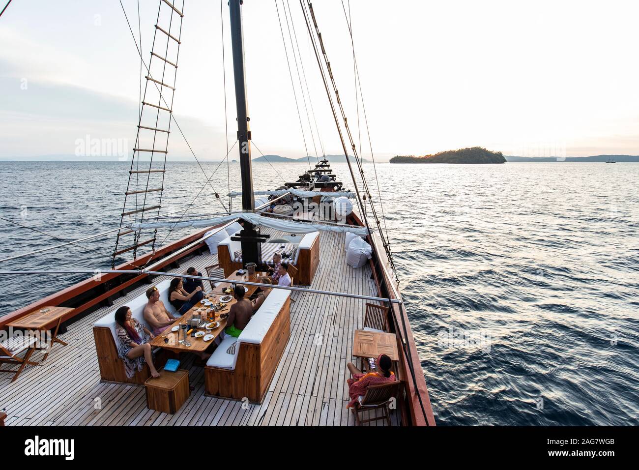 Guests dining on luxury phinisi sailing cruise boat at sunset in Raja ...