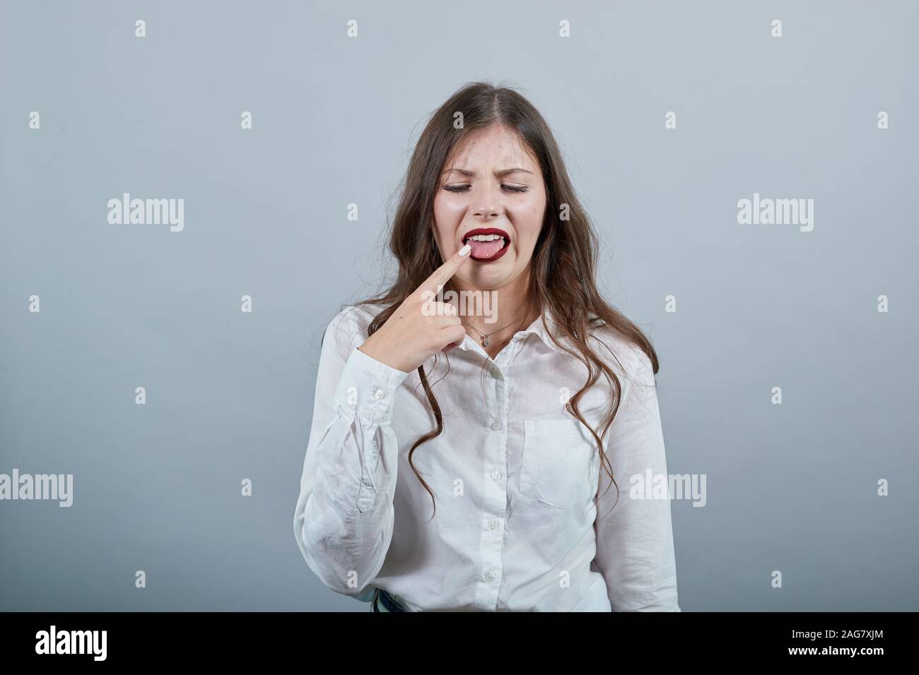Disappointed young woman keeping finger on tongue, looking confused ...