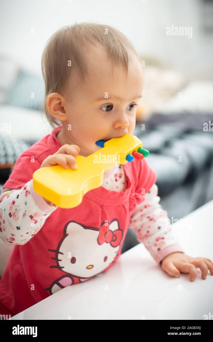 Cute caucasian 1 year old baby girl bites yellow guitar toy, concept of ...