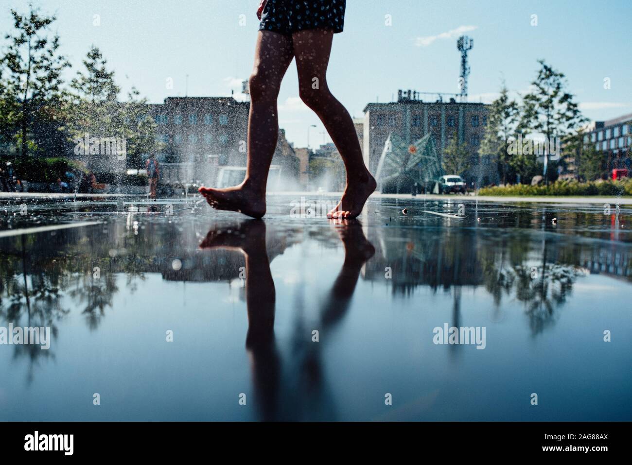 Reflection of a barefoot person on the wet sidewalk with water ...