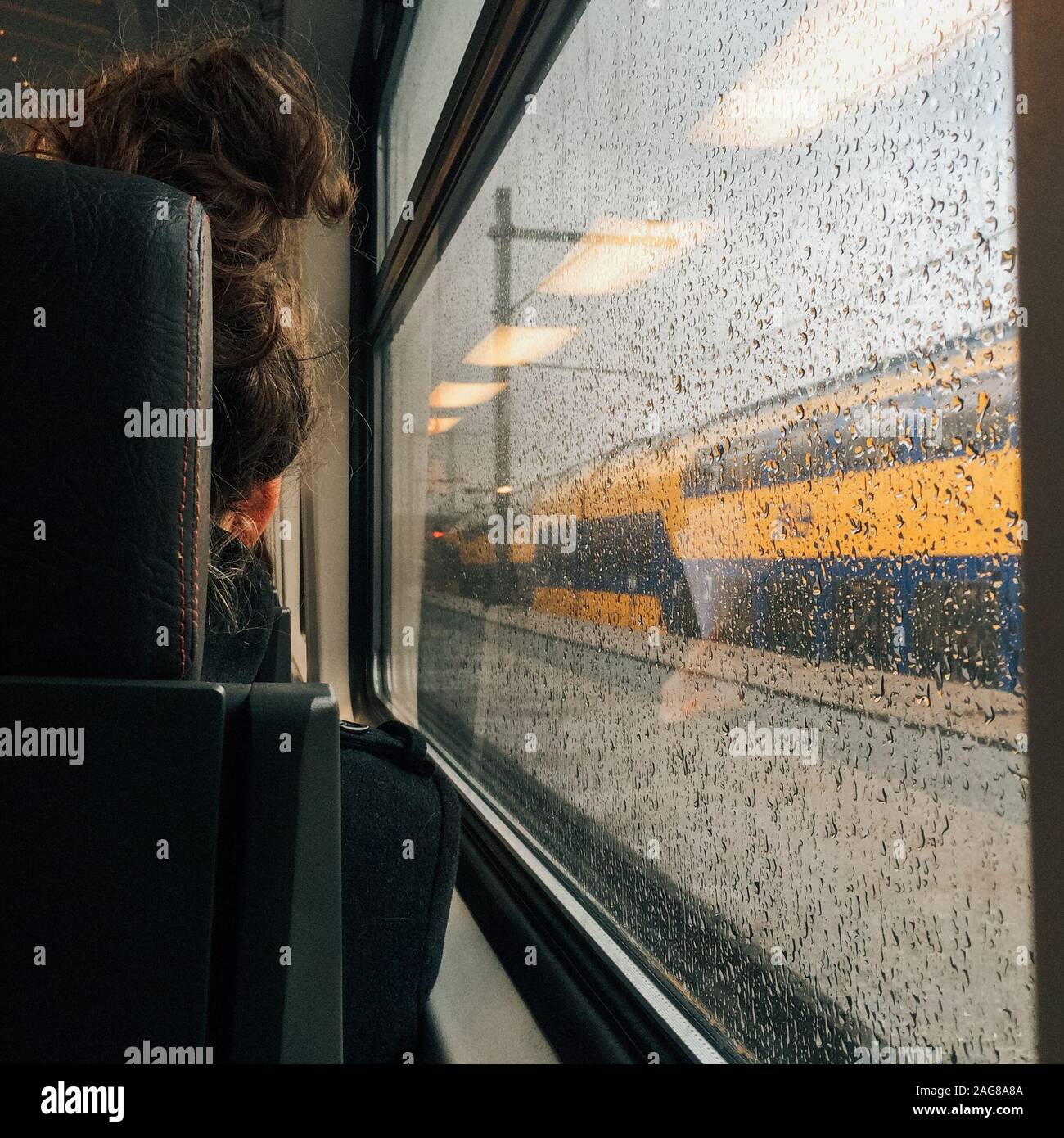 Female sitting in the train beside a window covered with water drops ...