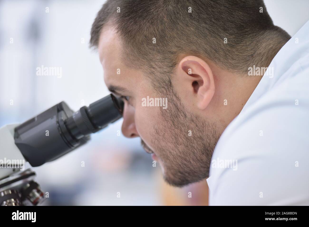 Young male scientist looking through a microscope in a laboratory doing ...