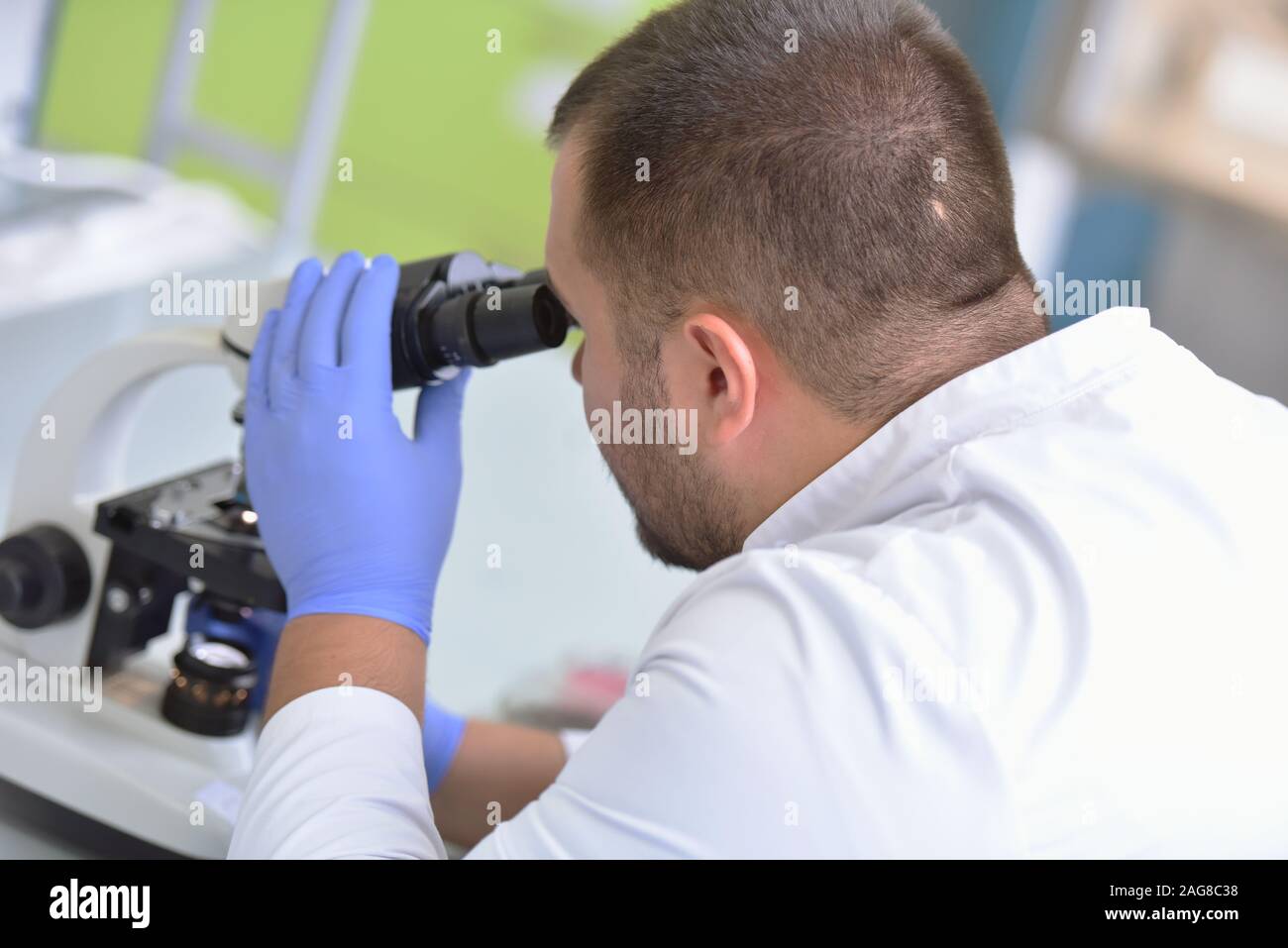 Young male scientist looking through a microscope in a laboratory doing ...