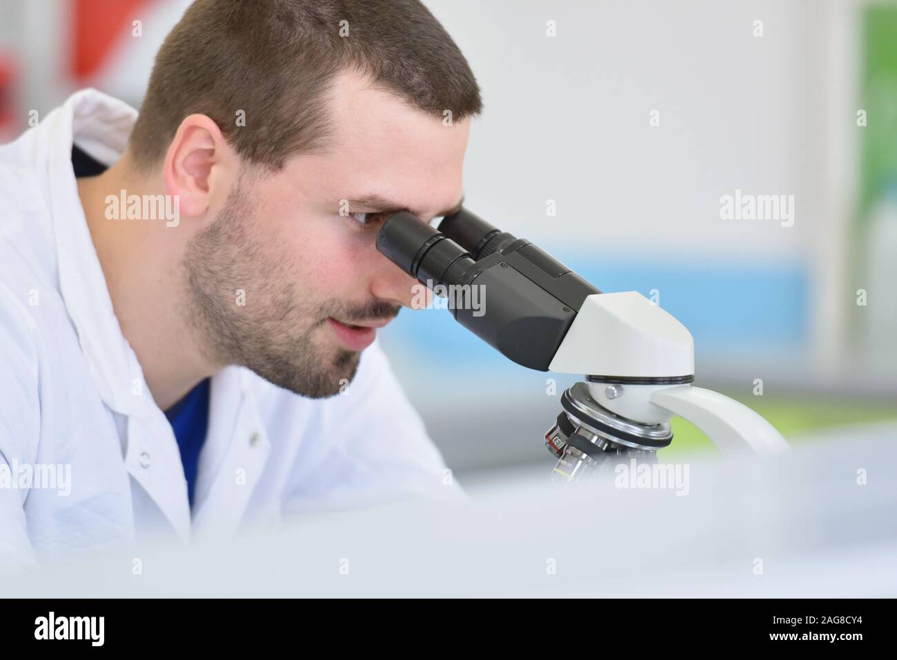 Young male scientist looking through a microscope in a laboratory doing ...