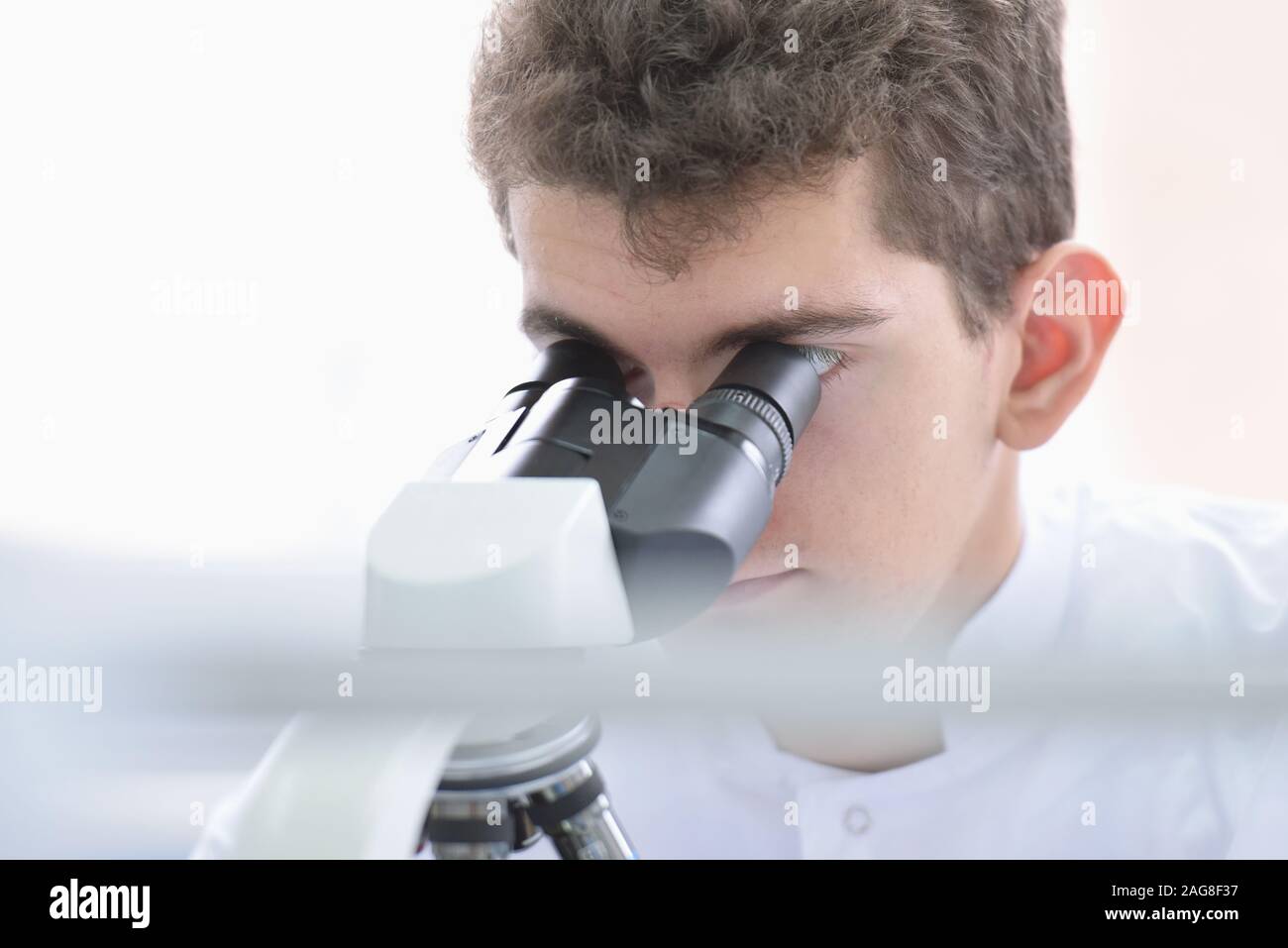 Young male scientist looking through a microscope in a laboratory doing ...