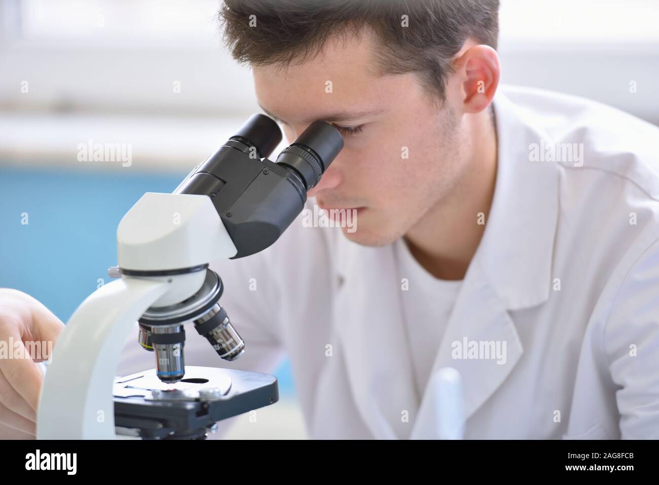 Young male scientist looking through a microscope in a laboratory doing ...
