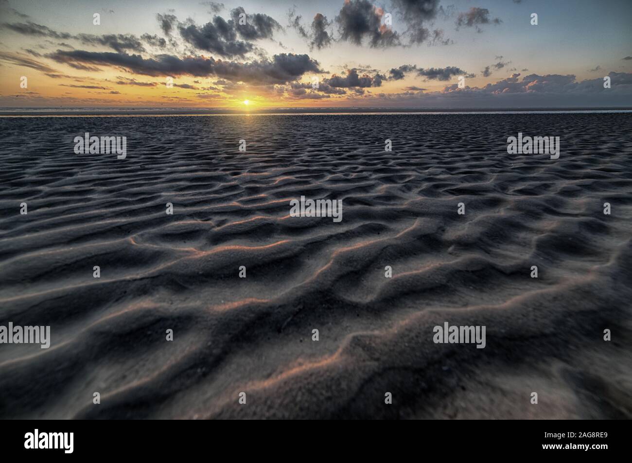 Beautiful scenery of the sunset reflected in a mudflat under the cloudy ...