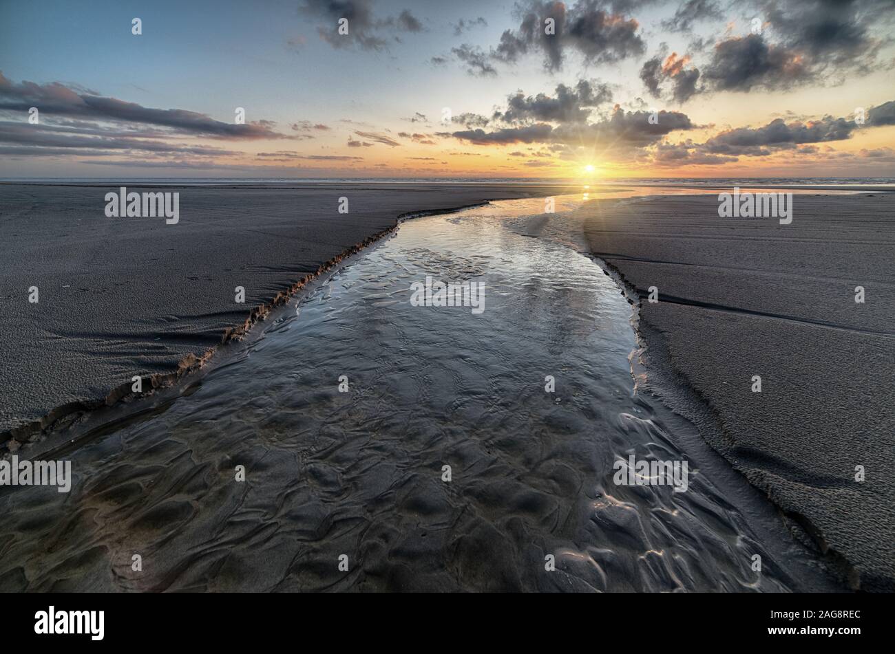 Beautiful scenery of the sunset reflected in a mudflat under the cloudy ...